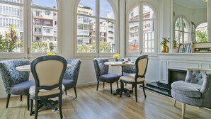 Quarto com lareira, janelas em arco amplas e cadeiras com padrão.