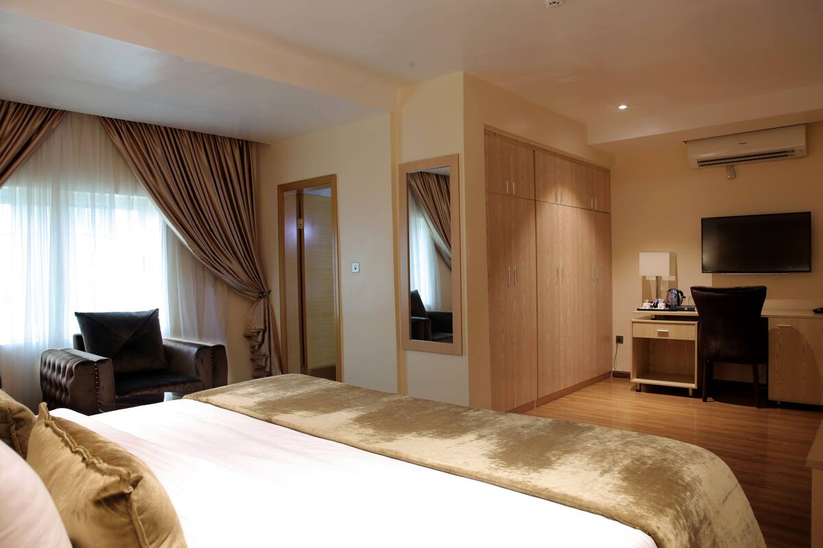 Quarto de hotel com uma cama, escrivaninha, cadeira, armário e televisão.