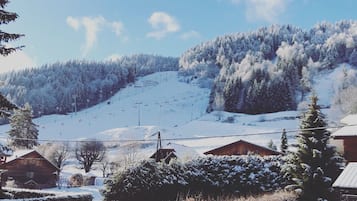 Paisagem montanhosa coberta de neve, com pista de esqui, cabanas de madeira e céu claro.