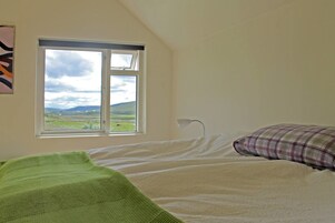 Quarto com uma cama, janela com vista para a paisagem e uma luminária.