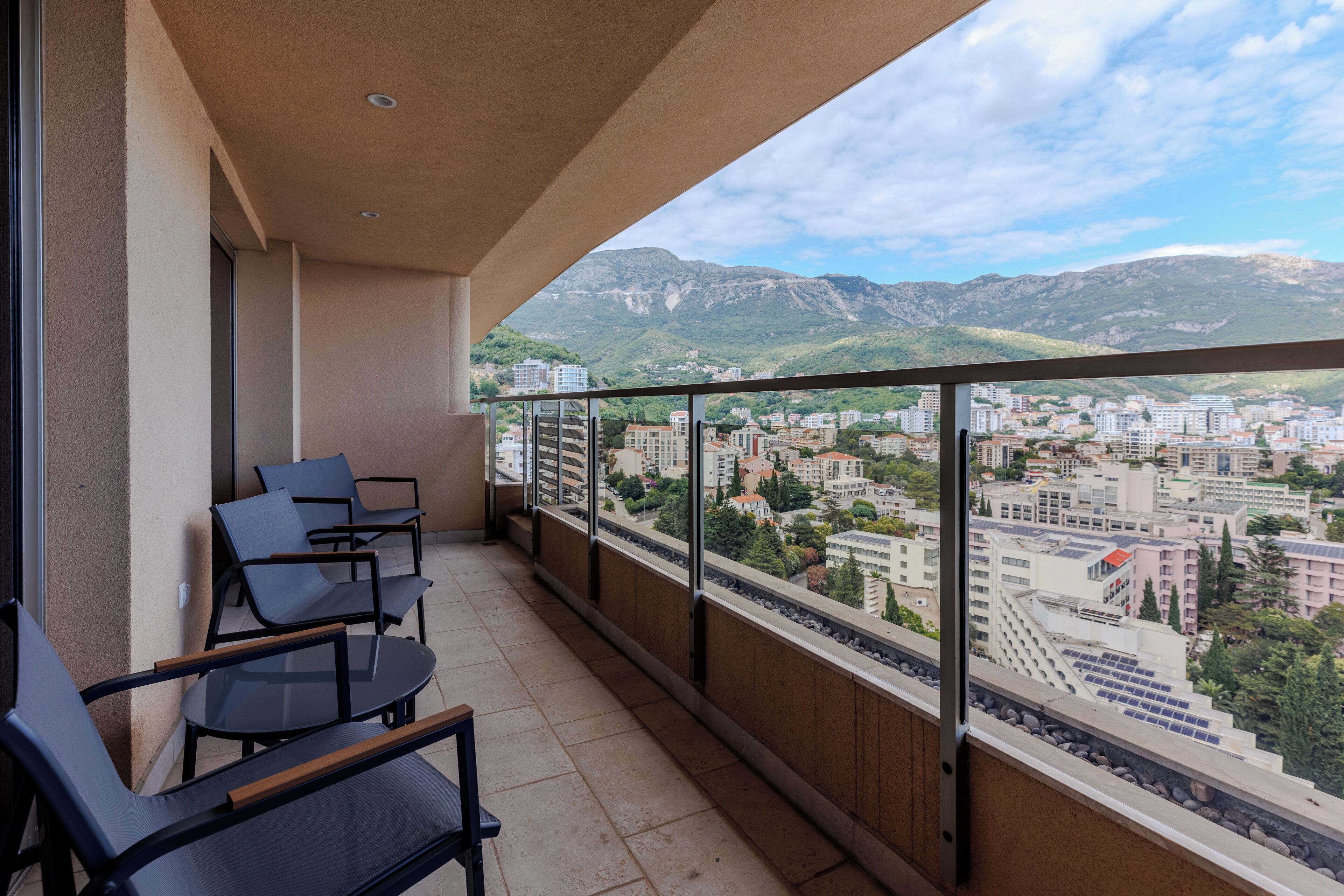 Varanda com vista para a cidade e montanhas. Há duas cadeiras e uma mesa na varanda.