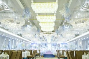 Um salão de banquetes com várias luminárias, mesas e cadeiras dispostas para um evento formal.