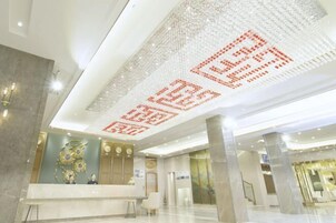 Um lobby de hotel moderno com balcão de recepção, teto decorativo imponente e piso limpo e bem cuidado.