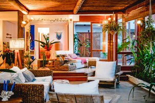 Um quarto aconchegante e bem iluminado, com móveis de vime, uma cama e diversas plantas.