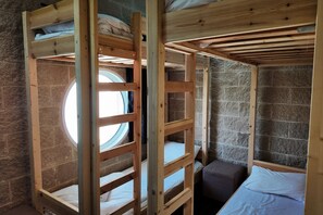 Quarto com beliche, claraboia, paredes de pedra e um pequeno banco.