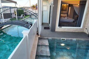 Quarto de hotel moderno com varanda envidraçada, piscina com deck de madeira e vista da região circundante.