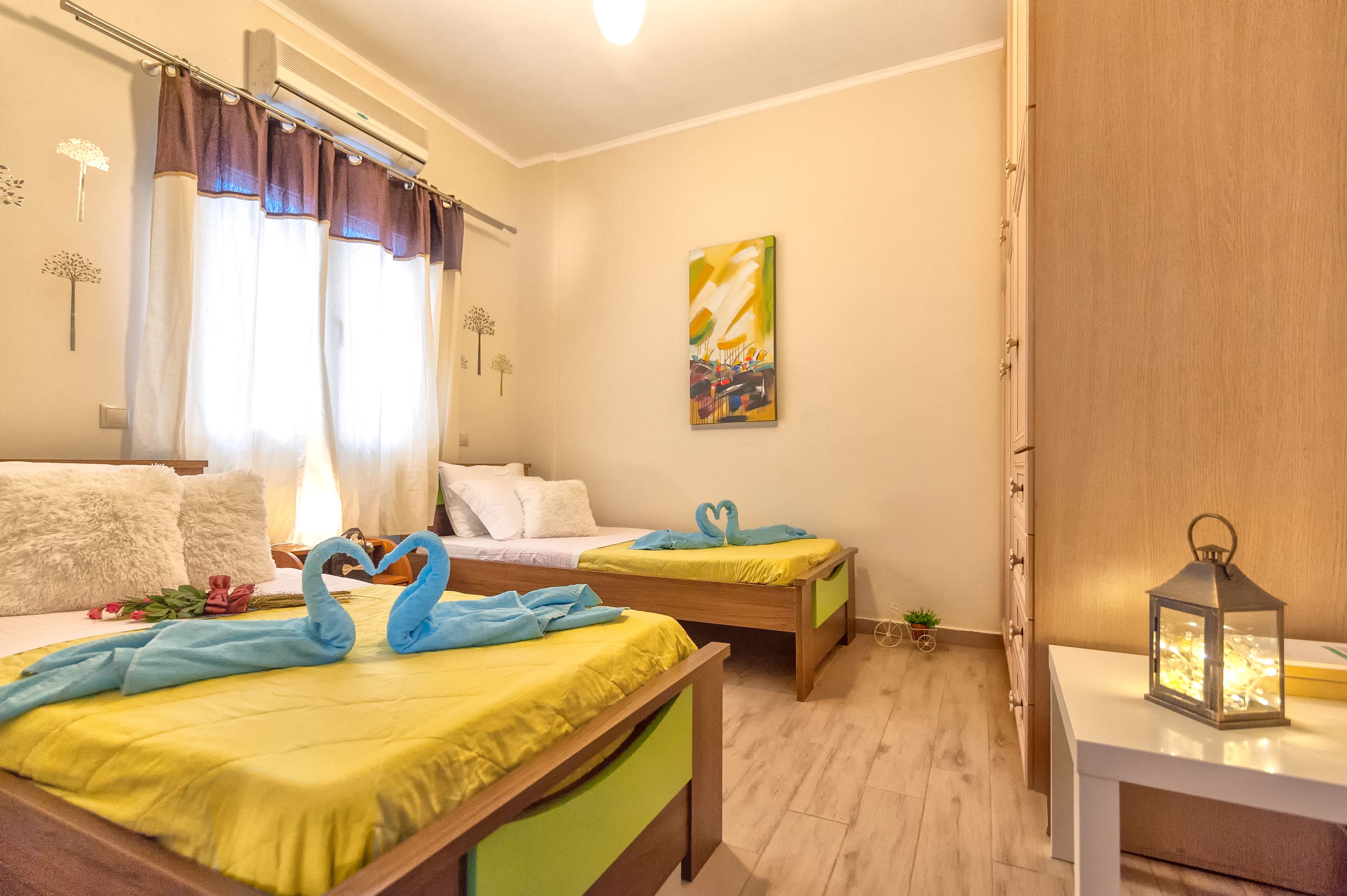 Quarto de hotel com duas camas, chão de madeira, um quadro na parede e um candeeiro sobre uma mesa.
