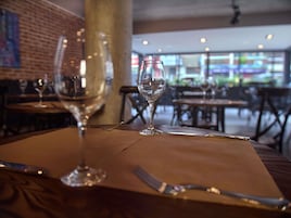 Interior de restaurante com mesas preparadas para refeições, apresentando copos e talheres cristalinos.