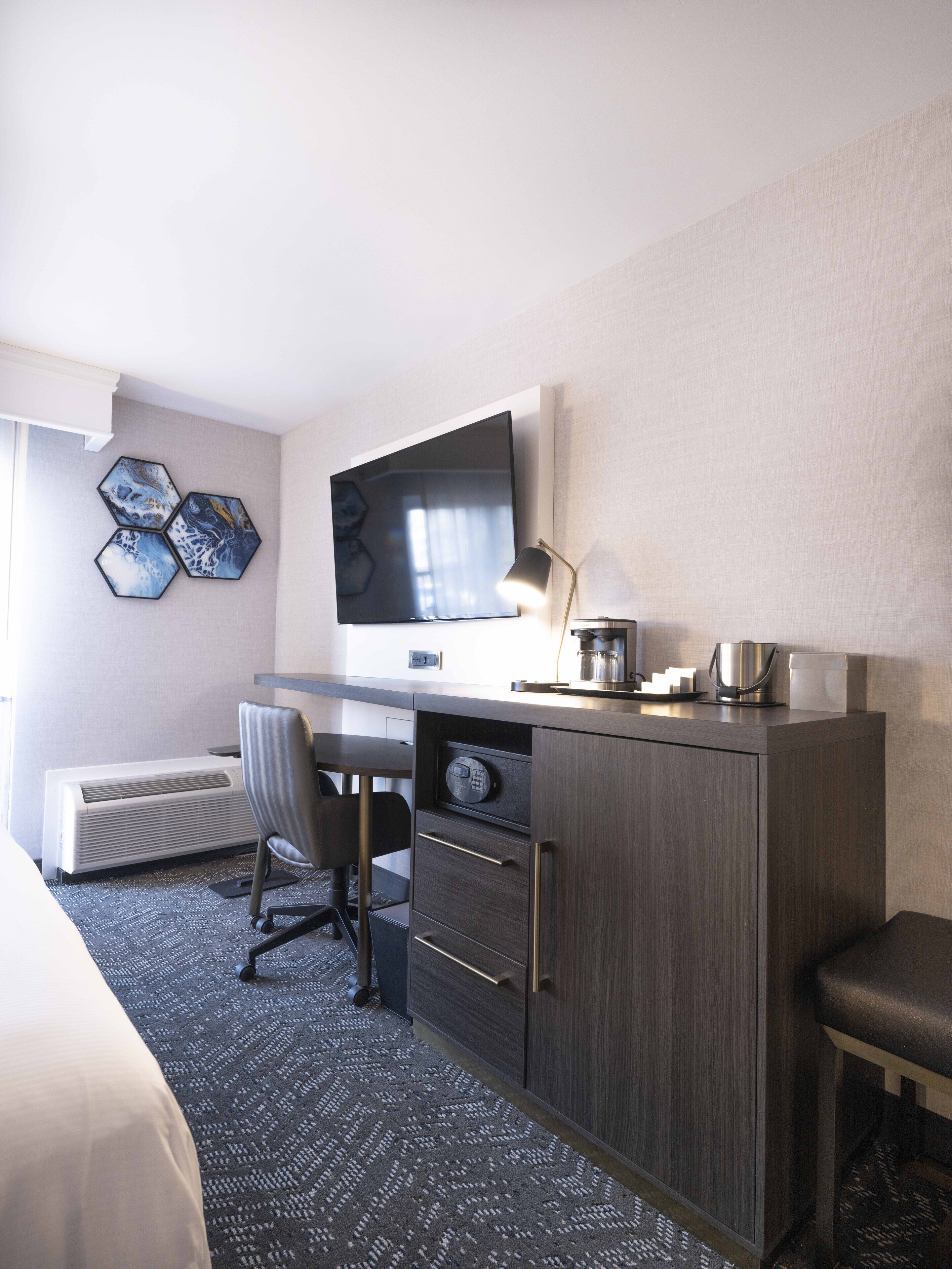 Quarto de hotel com cama, escrivaninha, cadeira, televisão, máquina de café e aquecedor.