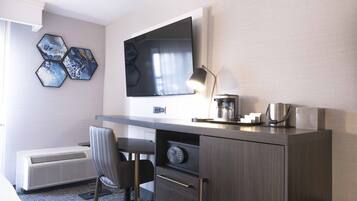 Quarto de hotel com cama, escrivaninha, cadeira, televisão, máquina de café e aquecedor.