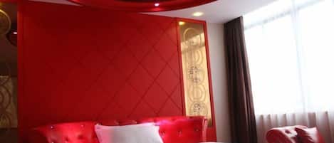 Quarto de hotel com cabeceira estofada em vermelho, espaldar branco e poltrona de couro vermelha.