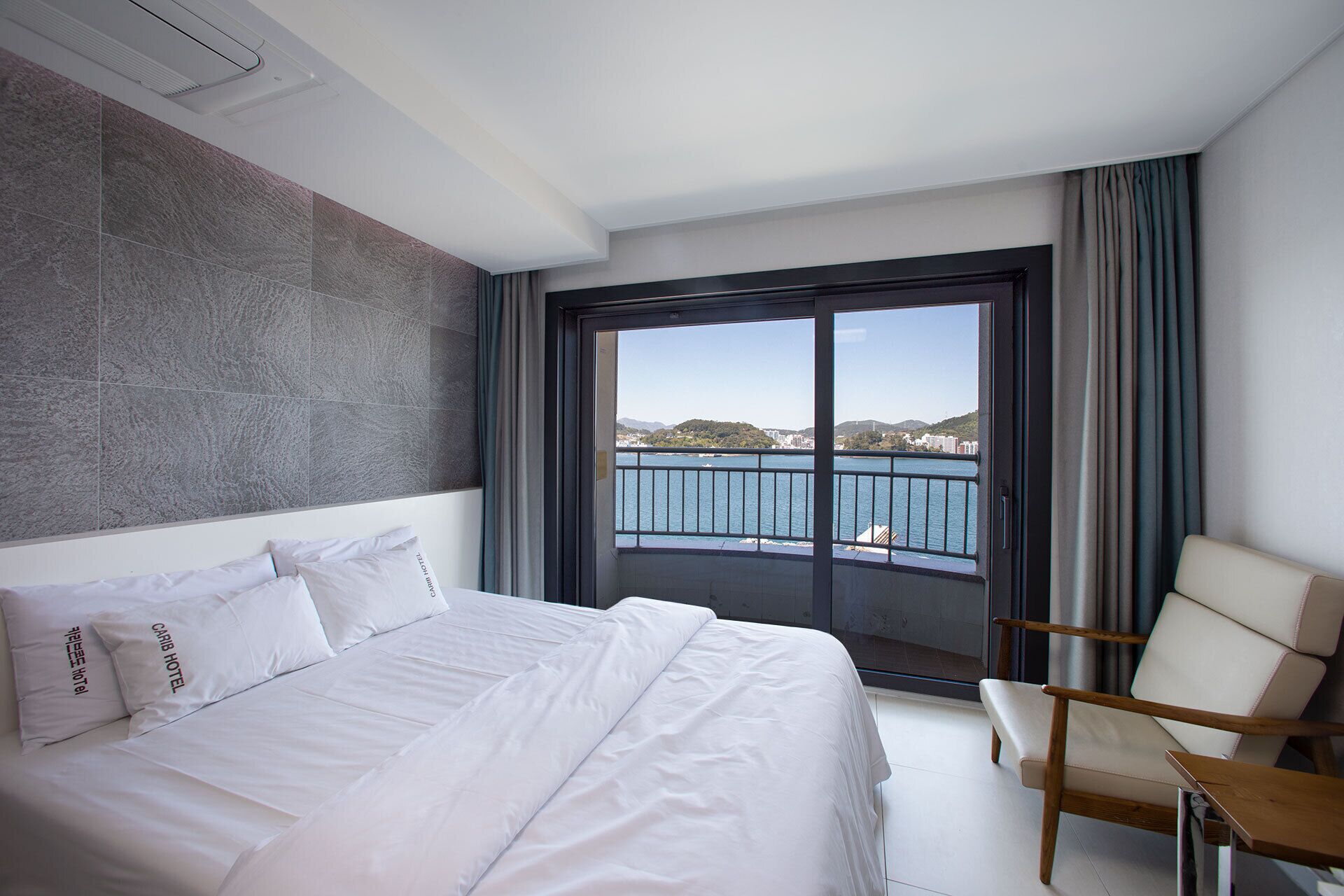 Quarto de hotel com uma cama grande, uma cadeira e vista para a água e edifícios.