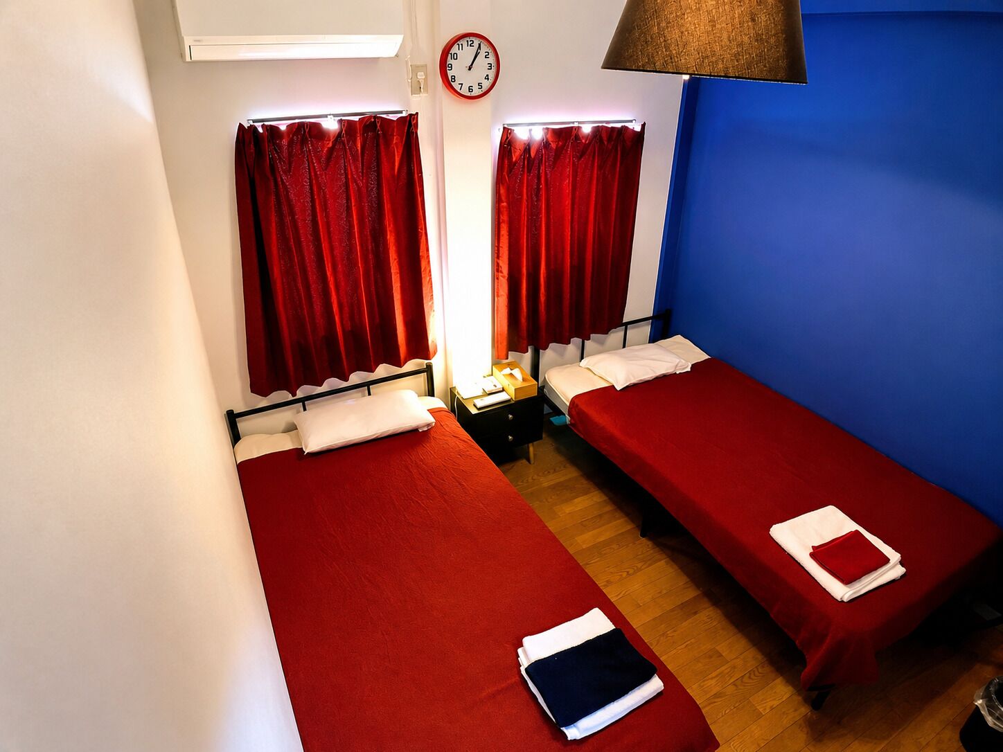 Quarto com duas camas, um relógio, uma mesa de cabeceira e uma luminária.