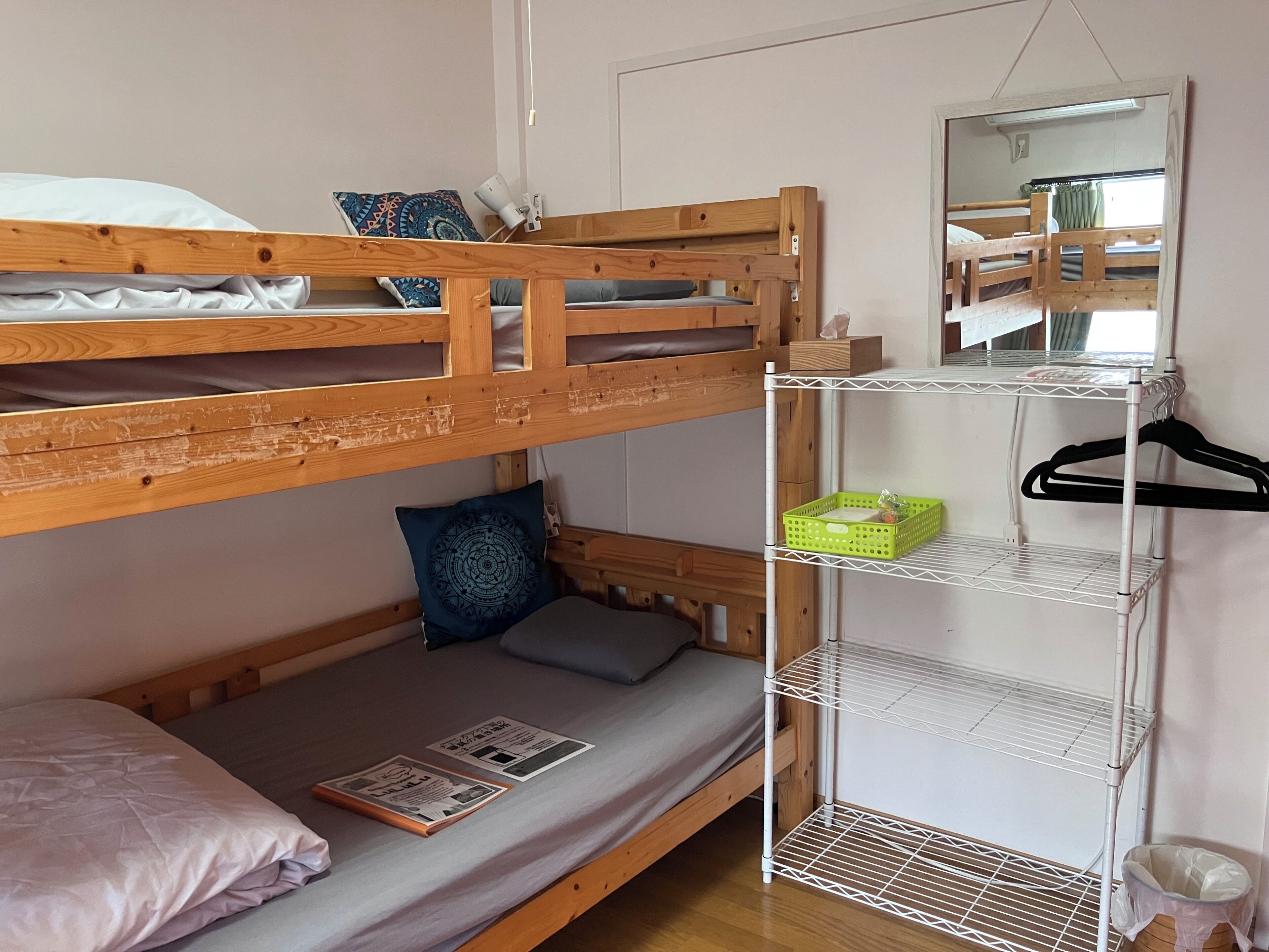 Uma cama beliche com uma cama na parte inferior, uma estante com espelho e uma pequena lixeira.