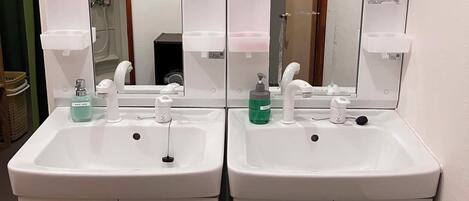 Casa de banho com duas lavatórios, cada uma com espelho acima. Existem dispensadores de sabonete líquido e um porta-toalhas com uma toalha laranja.