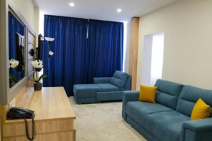 Quarto com sofá azul, escrivaninha de madeira com telefone e espelho com planta.