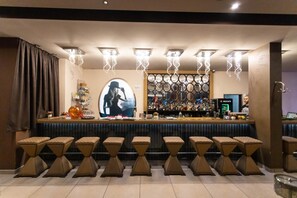 Uma área de bar com balcão, banquetas e um espelho decorativo.