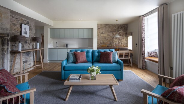Uma sala de estar moderna com um sofá azul, mesa de centro de madeira e uma parede de pedra.