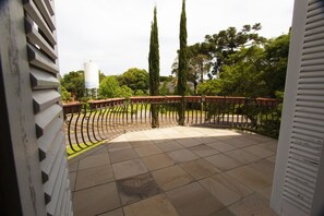 Um pátio com piso de azulejos, cerca de metal e árvores altas.