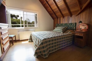 Quarto com uma janela grande, cama com colcha xadrez, mesa de cabeceira com espelho e cabeceira de madeira.