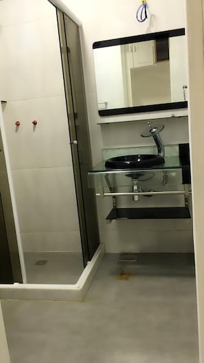 Casa de banho com cabine de duche em vidro, lavatório com cuba preta e espelho sobre o lavatório.