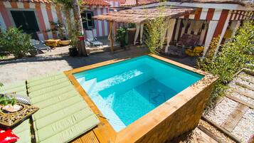 Piscina retangular com deck de madeira e espreguiçadeiras verdes.
