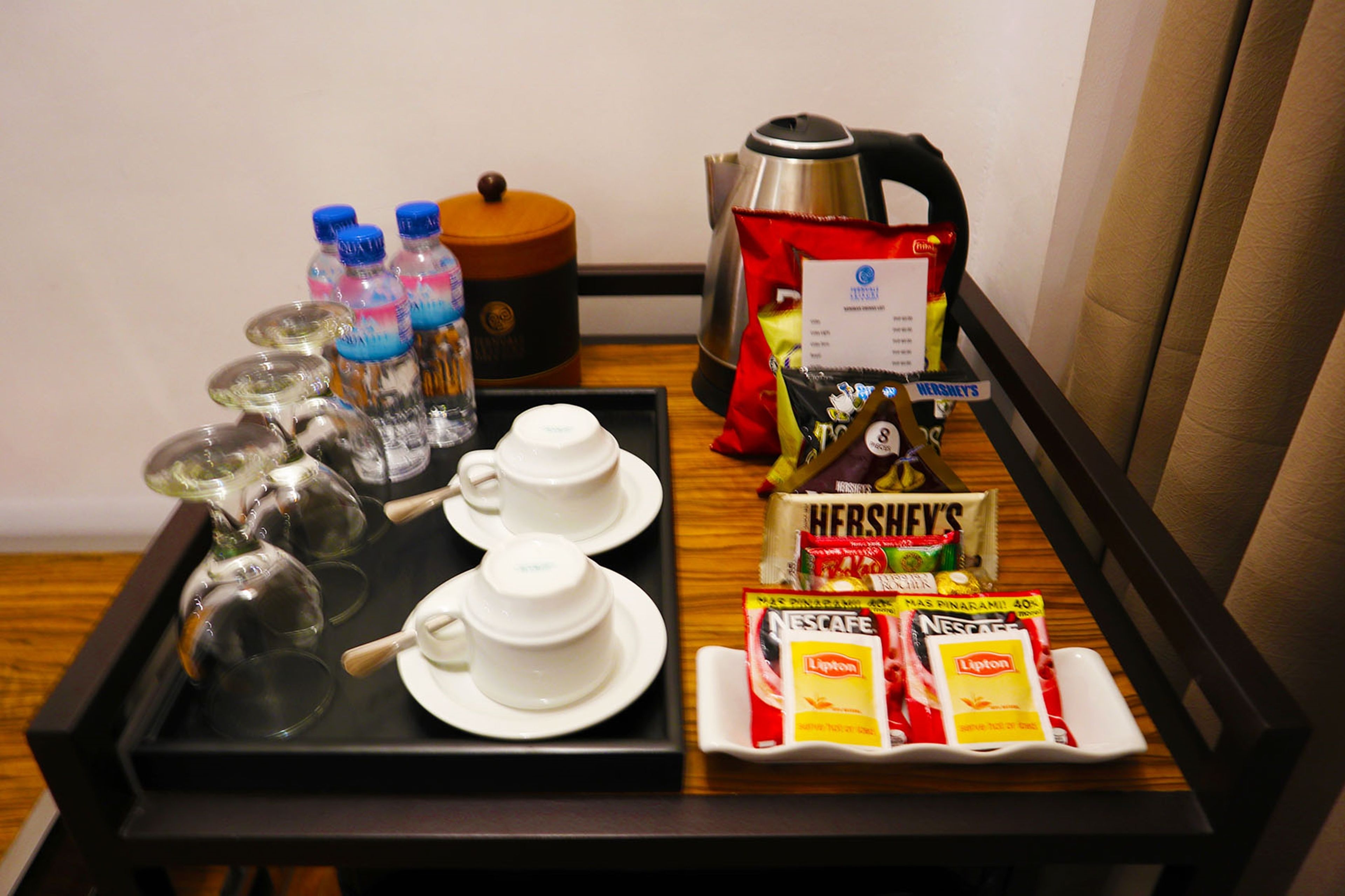 Uma bandeja com xícaras de café, chaleira, água engarrafada e lanches, incluindo chocolate Hershey's e café Nescafé.