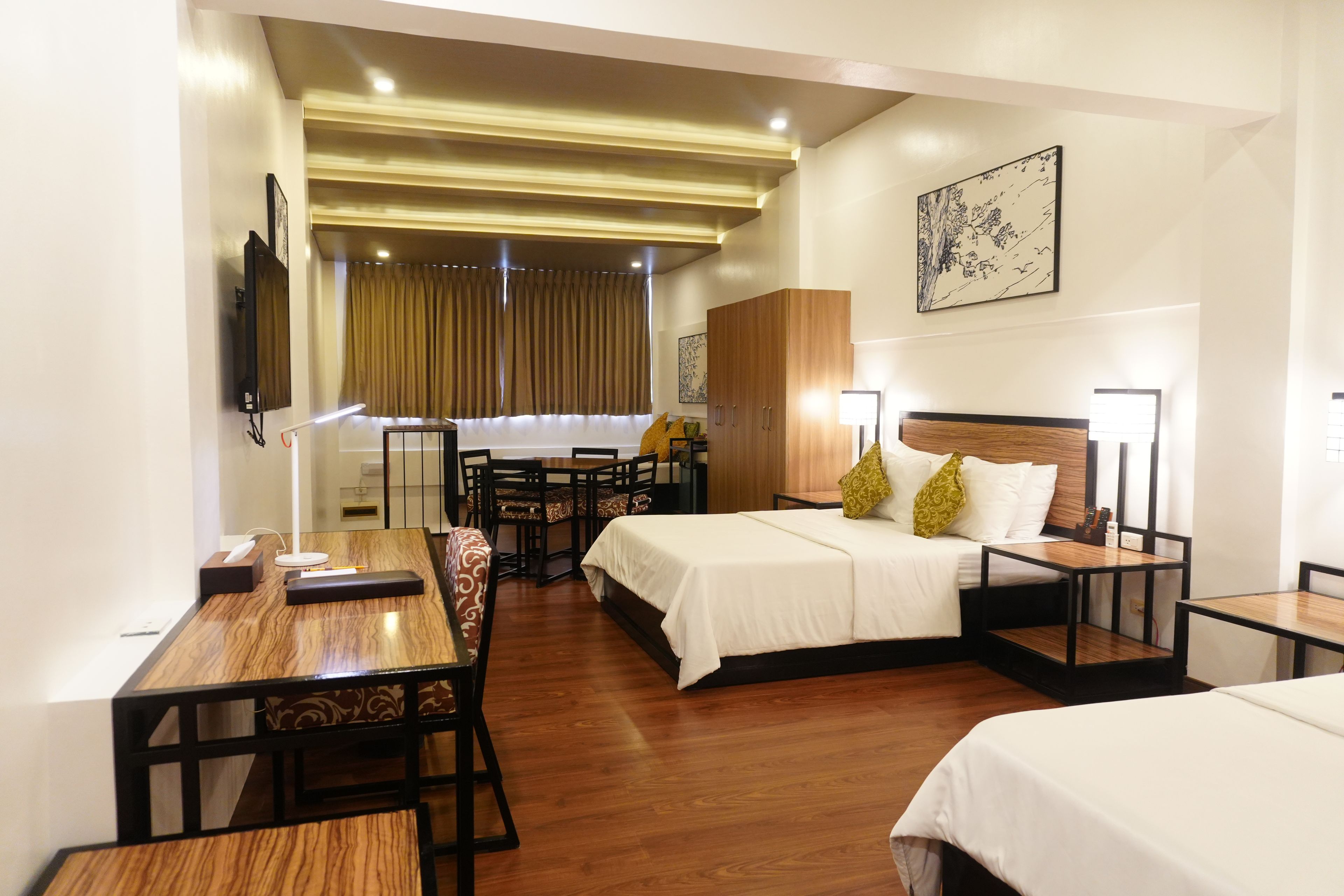 Quarto de hotel com cama, mesas de cabeceira, escrivaninha, cadeira, televisão e janela com cortinas.