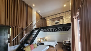 Quarto de hotel com escada, uma cama, escrivaninha e uma mesinha.