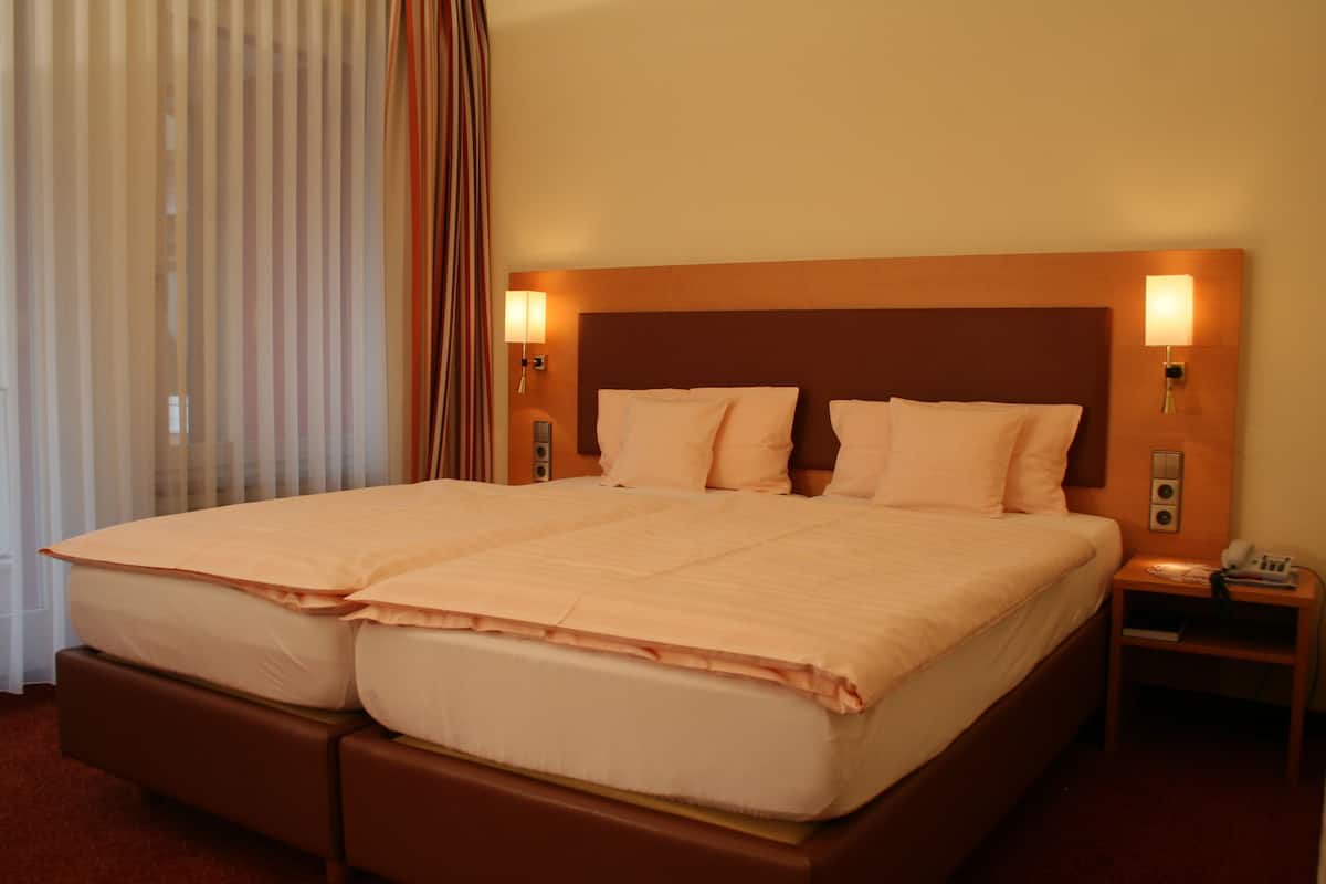 Uma cama de casal com cabeceira de madeira, duas mesas de cabeceira com luminárias e uma janela com cortinas.