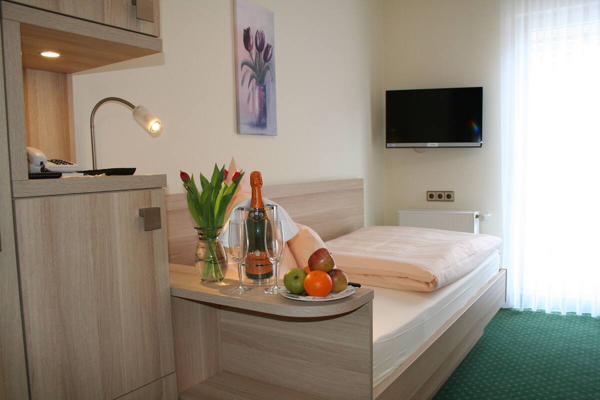 Quarto de hotel com cama, mesa de cabeceira, luminária, obras de arte, televisão e um prato de frutas.