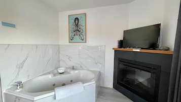 Uma casa de banho moderna com toucador em mármore, banheira, televisão montada e lareira.