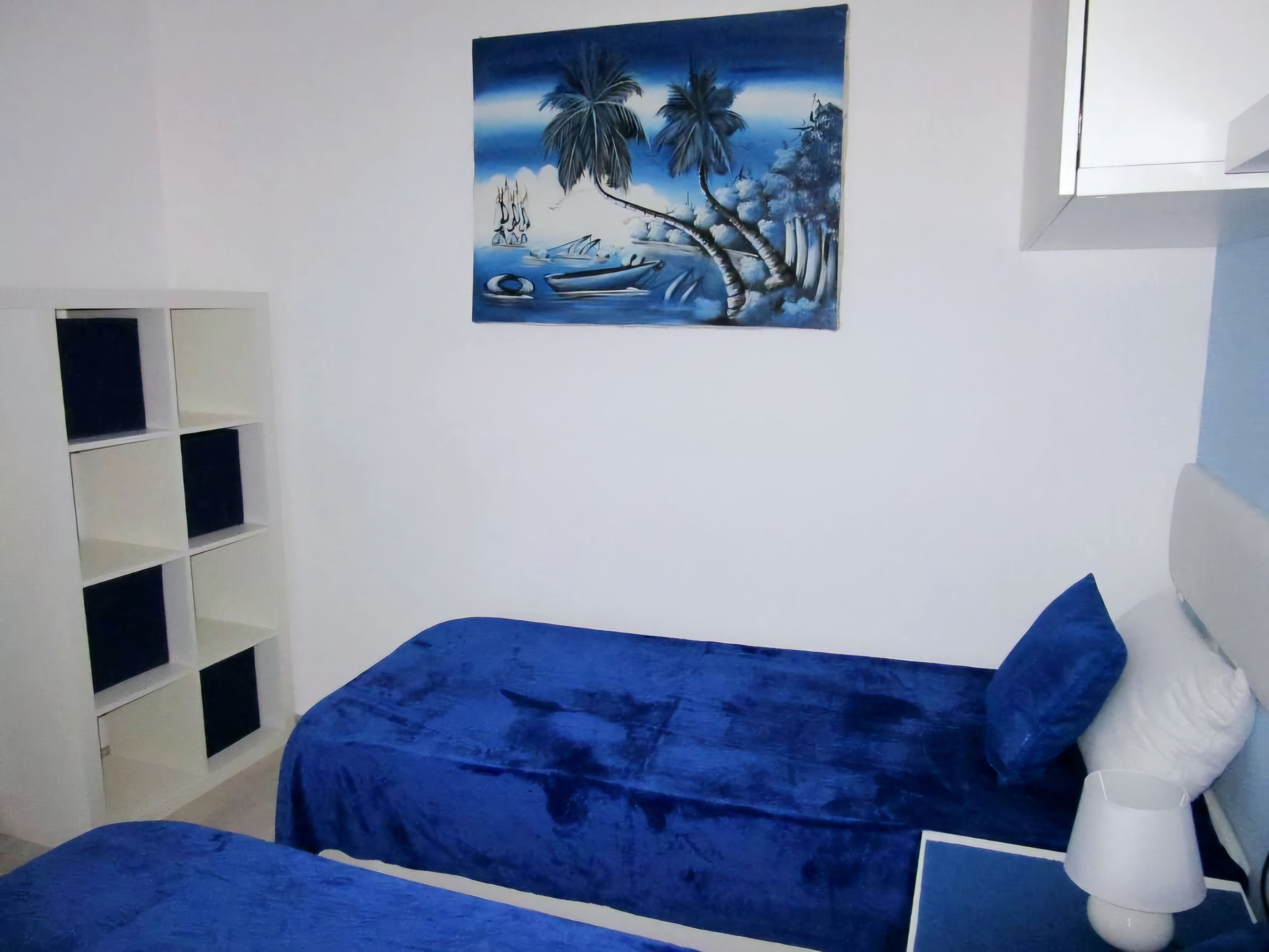 Quarto com duas camas, um guarda-roupa branco e um quadro de uma paisagem tropical.