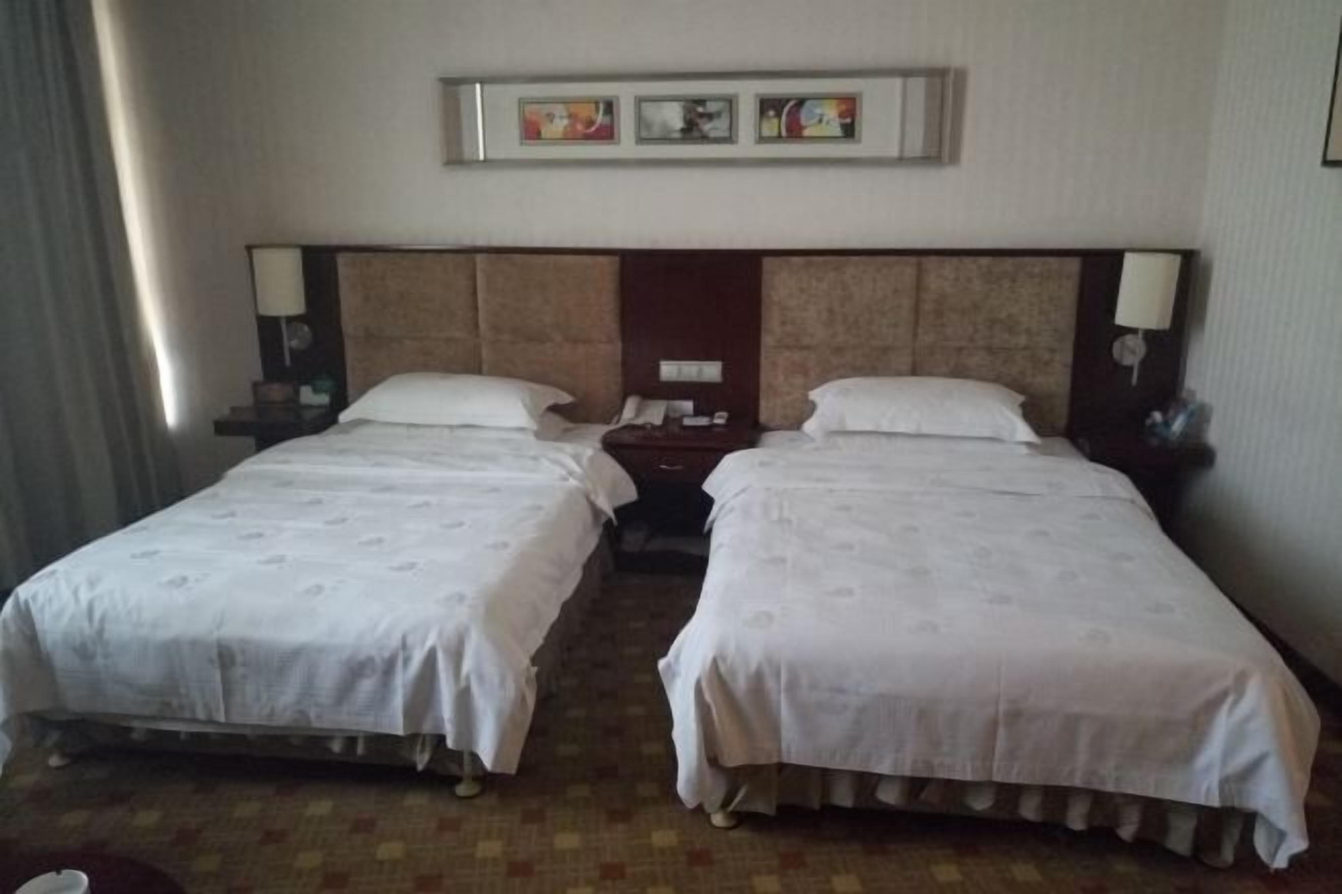 Quarto de hotel com duas camas de solteiro, mesa de cabeceira com abajur e uma mesinha com telefone.