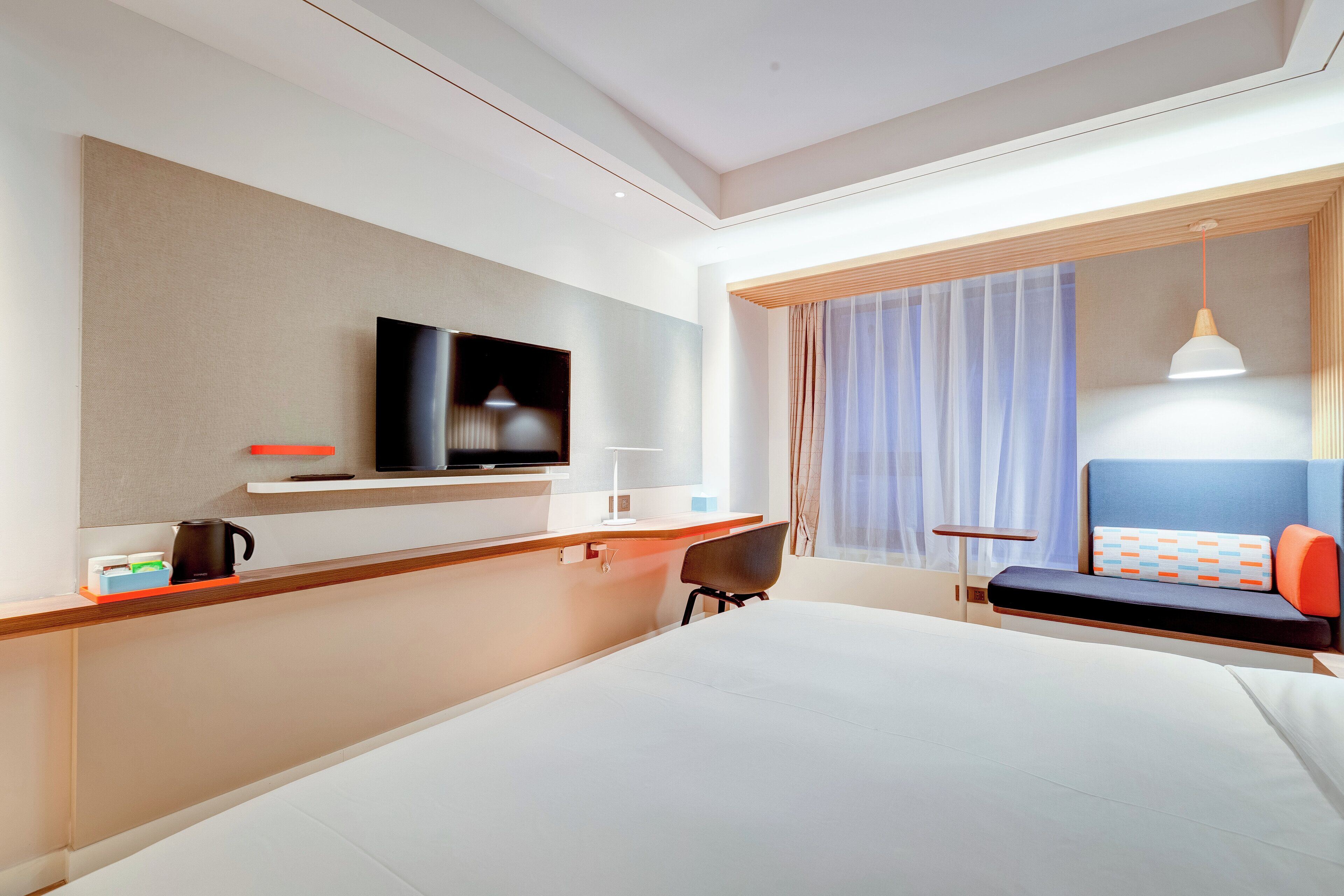 Quarto de hotel com cama, escrivaninha, televisão e janela com cortinas.