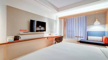 Quarto de hotel com cama, escrivaninha, televisão e janela com cortinas.