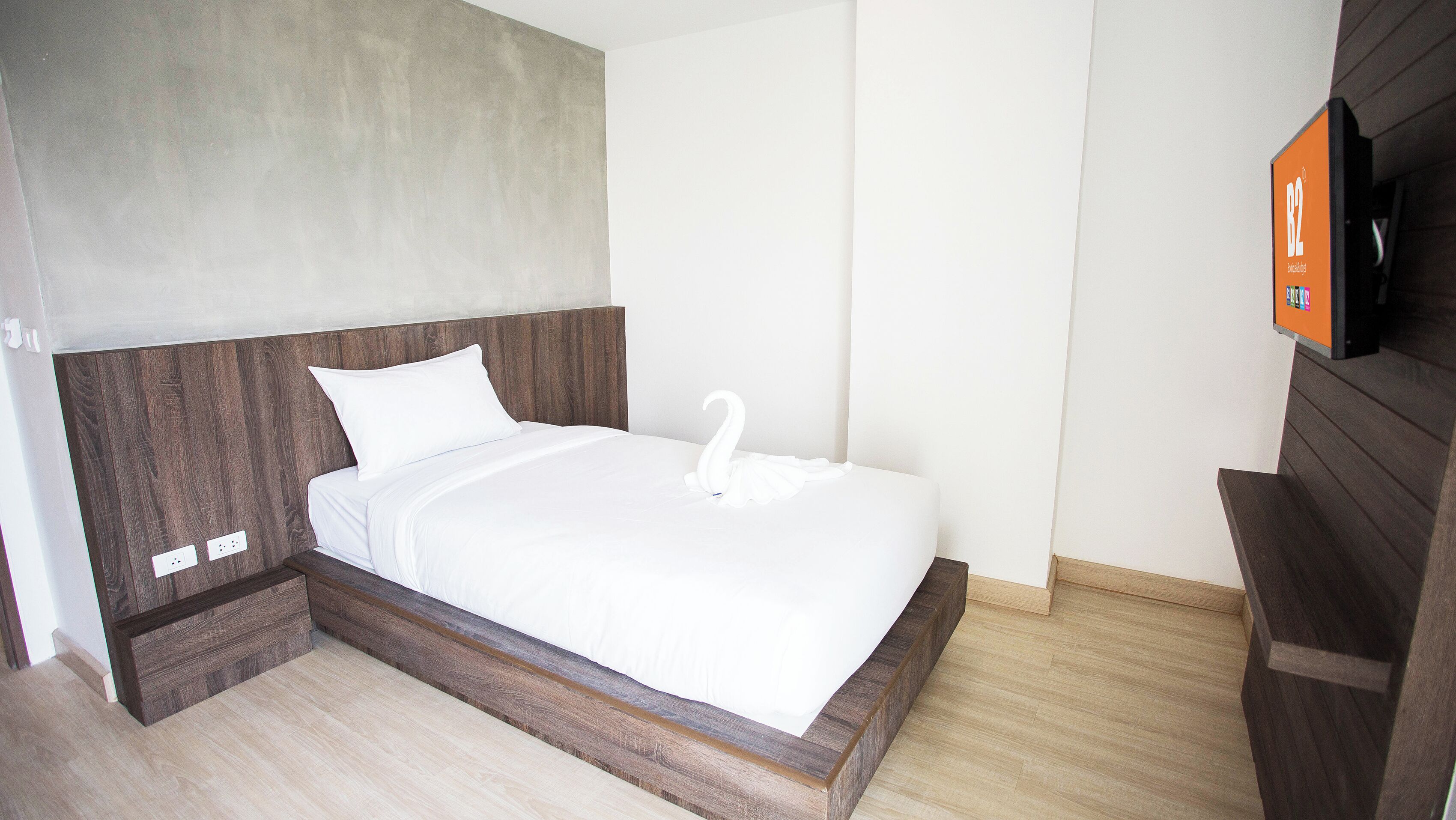 Quarto de hotel moderno com cabeceira de madeira, colcha branca e travesseiro em forma de cisne.