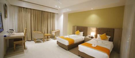 Quarto de hotel com duas camas, uma mesa, uma cadeira e uma janela grande com cortinas.