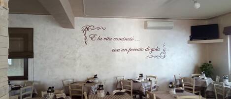 Interior de restaurante com toalhas de mesa quadriculadas, cadeiras de madeira e parede decorativa com texto em italiano.