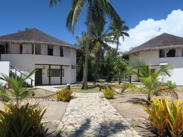 Um resort com duas cabanas de telhado de palha, um caminho de pedra e paisagismo tropical.