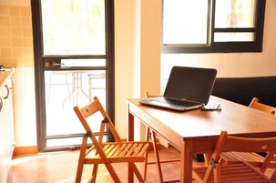 Quarto com uma mesa e cadeiras de madeira, um laptop e uma janela com vista para móveis de exterior.