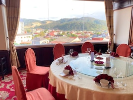 Uma área de refeições com uma mesa redonda posta para seis pessoas, com vista para uma paisagem pitoresca de uma cidade e colinas.