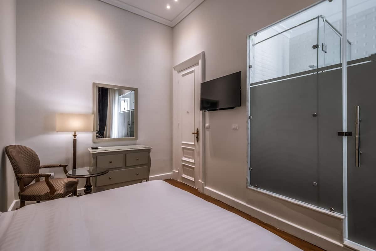 Quarto com uma cama grande, cômoda, cadeira, televisão e um closet espaçoso com porta deslizante.