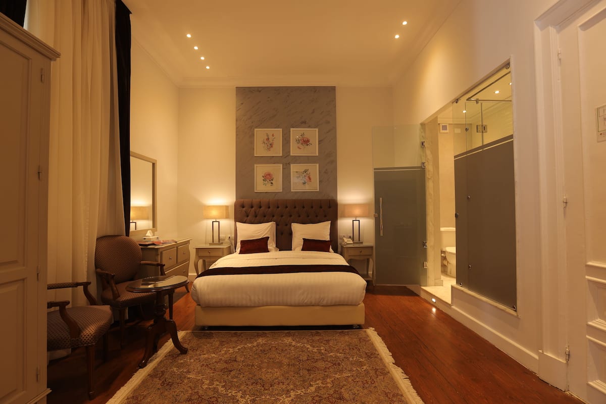 Quarto com cama grande, duas mesas de cabeceira, uma cadeira, um tapete e um espelho.