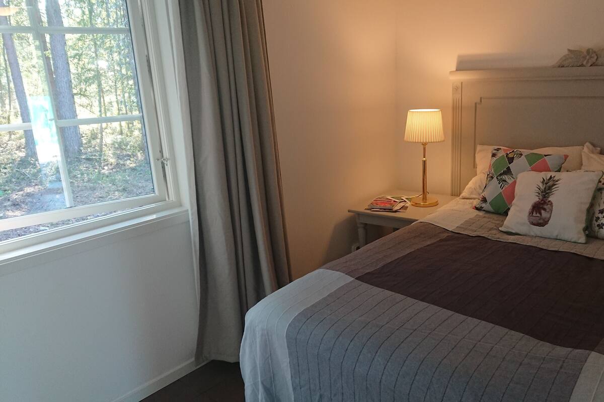 Quarto de hotel com cama, mesa de cabeceira, abajur e janela com cortinas.