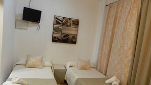 Quarto de hotel com duas camas de solteiro, uma TV fixada na parede e um quadro sobre as camas.
