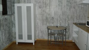 Cozinha compacta com armário branco, uma pequena mesa de jantar com duas cadeiras, micro-ondas e televisão na parede.