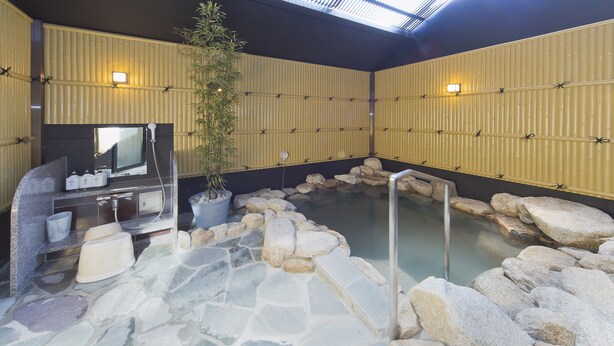 Uma onsen japonesa tradicional com uma nascente de pedra, paredes de bambu e uma planta em vaso.