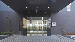 Uma entrada de edif ício moderna com porta de vidro, piso ladrilhado e uma placa.