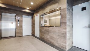 Área de elevador moderna com parede de mármore, parede espelhada e chão revestido de azulejos.